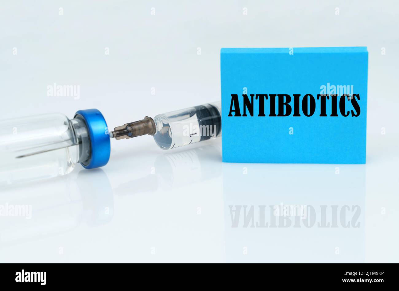 Medical concept. On a white reflective surface there is a syringe with ...