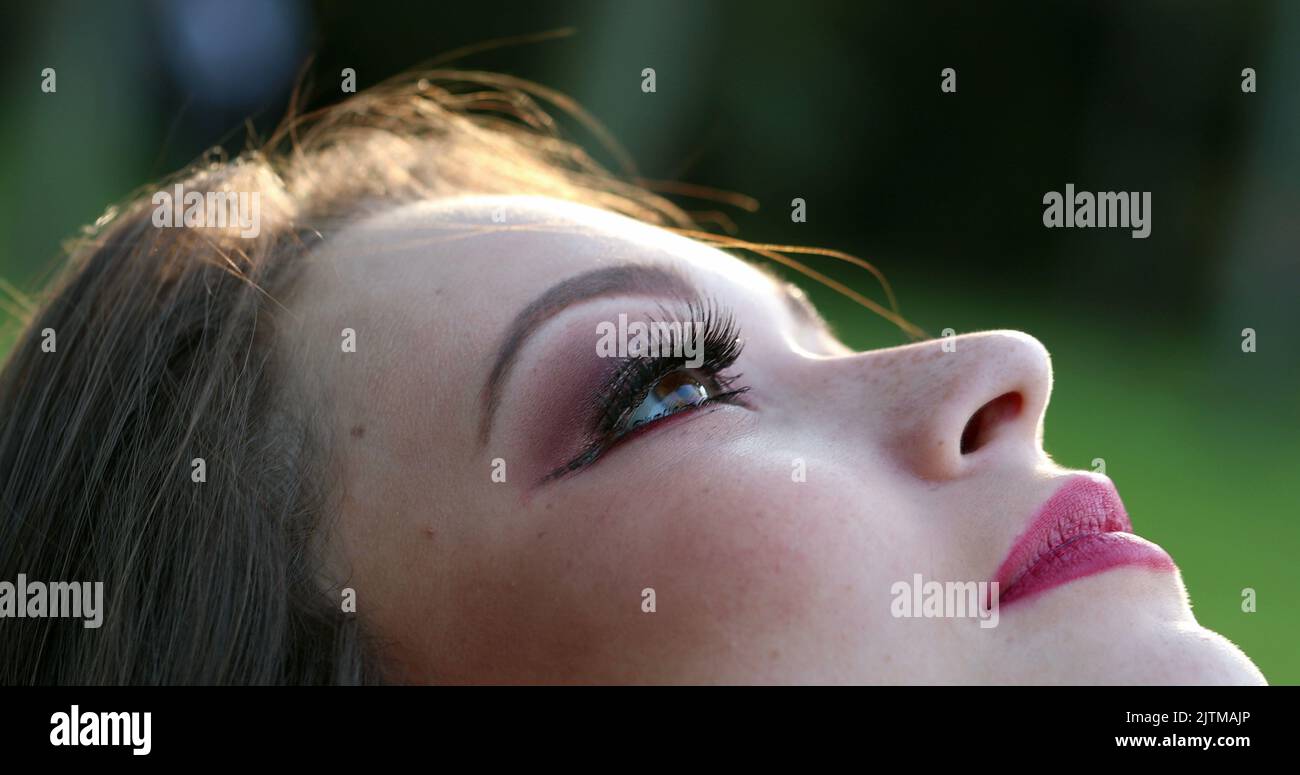Attractive young woman face opening eyes looking at the sky with hope ...