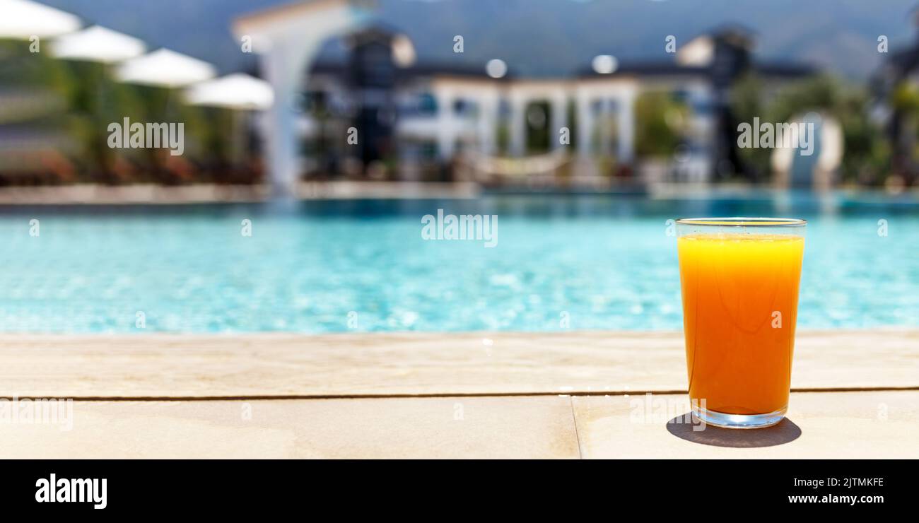 Glass of fresh cool orange juice drink on swimming pool board, summer ...