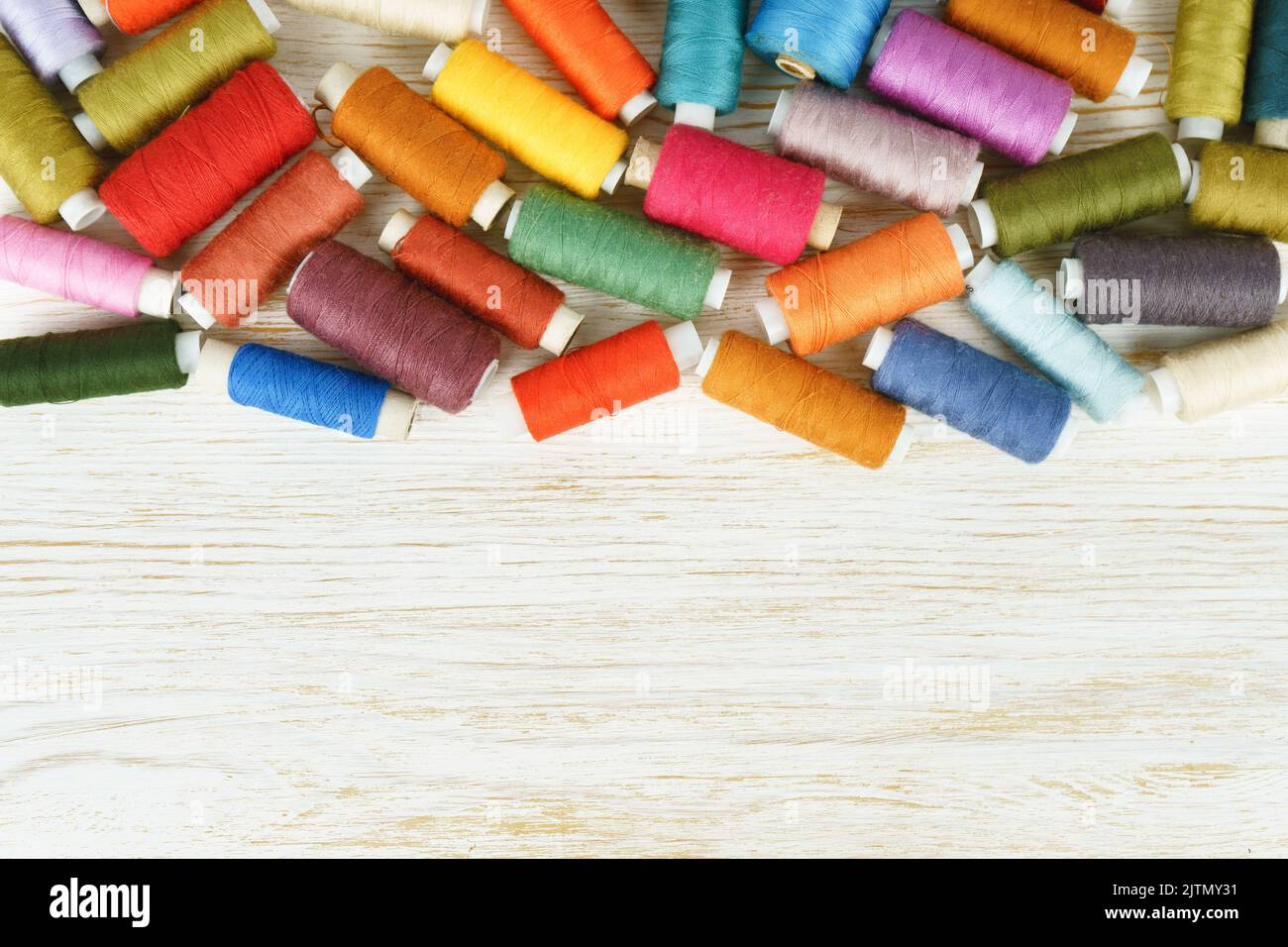 Scattering of various colors sewing threads on white wooden background ...