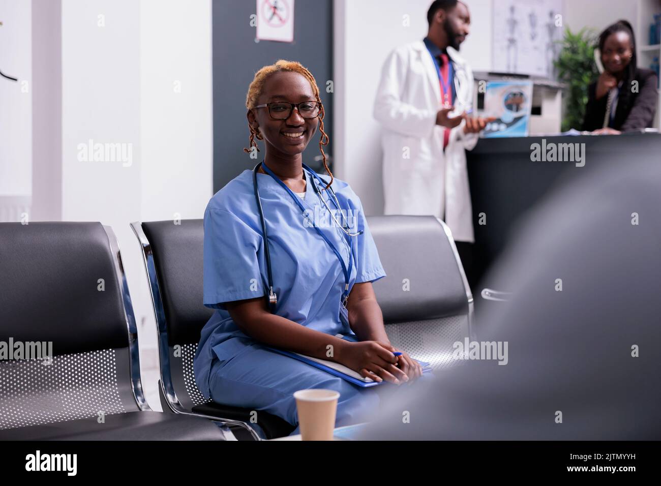 Portrait of female nurse in waiting area, sitting in hospital lobby ...