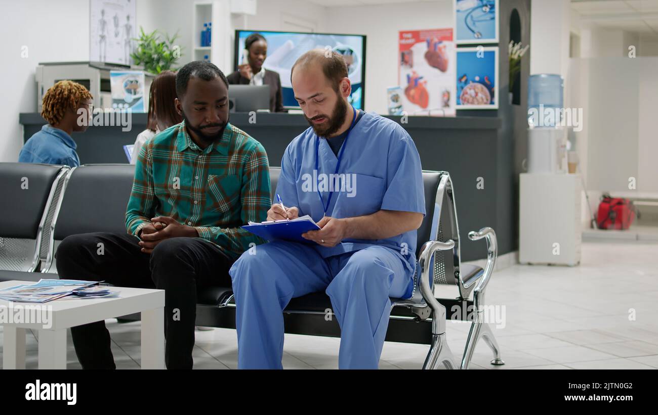 Male nurse talking to african american man in waiting room lobby, doing ...
