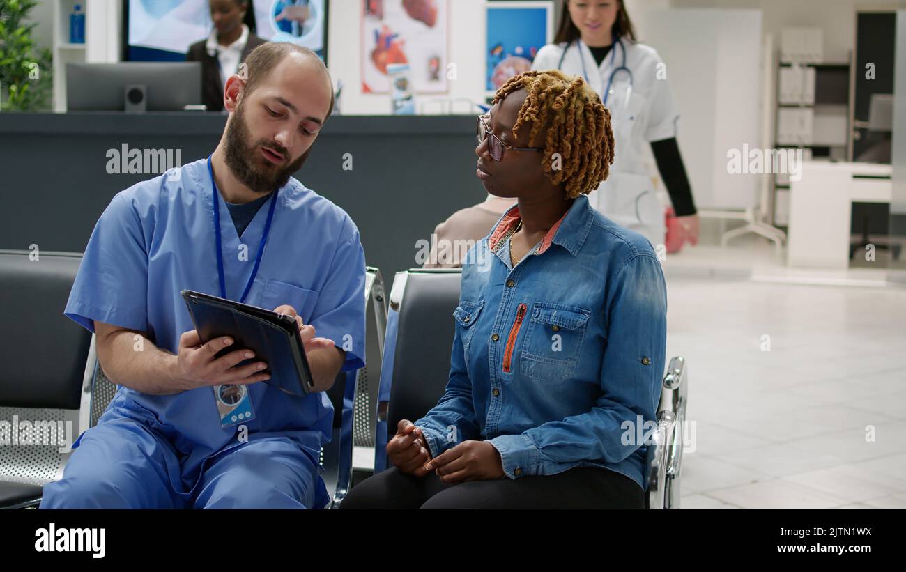 Female patient and medical assistant looking at digital tablet to talk ...