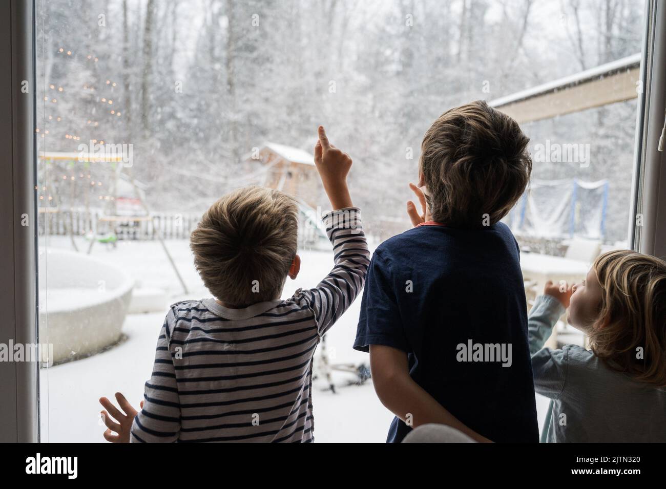 Three siblings, brothers and sister, looking out the window amazed by ...