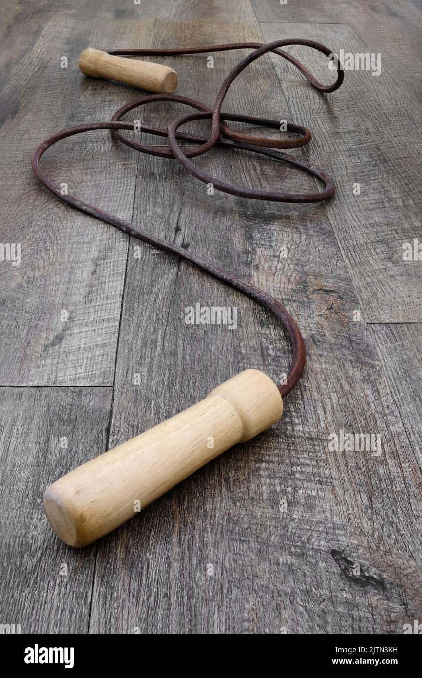Old leather skipping rope with wooden handles coiled on a wooden floor ...