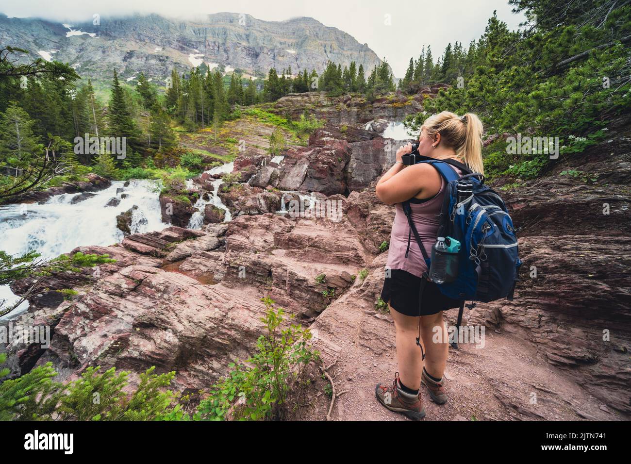 Blonde hiker woman takes photos at Redrock Falls along Swiftcurrent ...