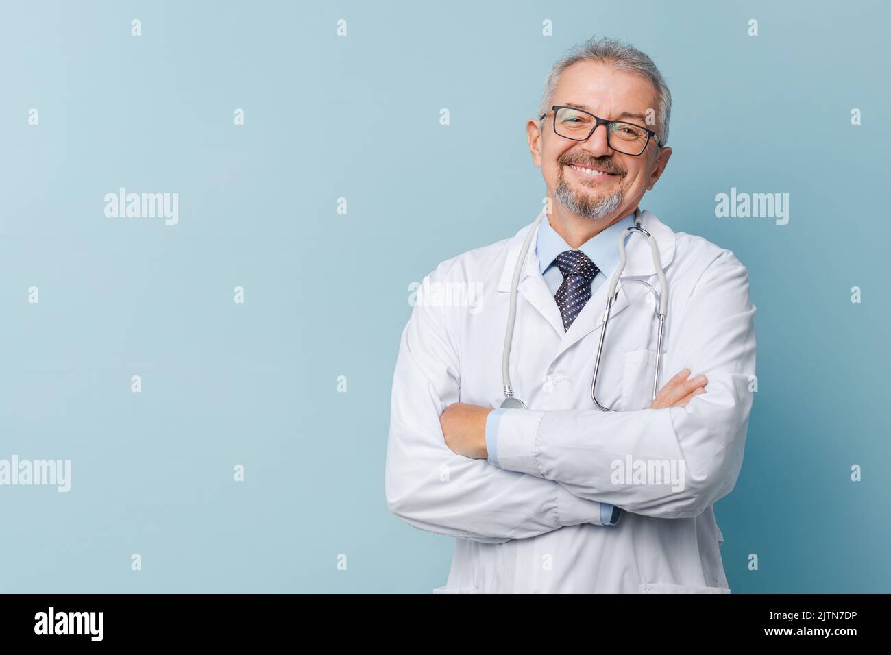 Smiling male doctor in lab coat with arms crossed against blue ...
