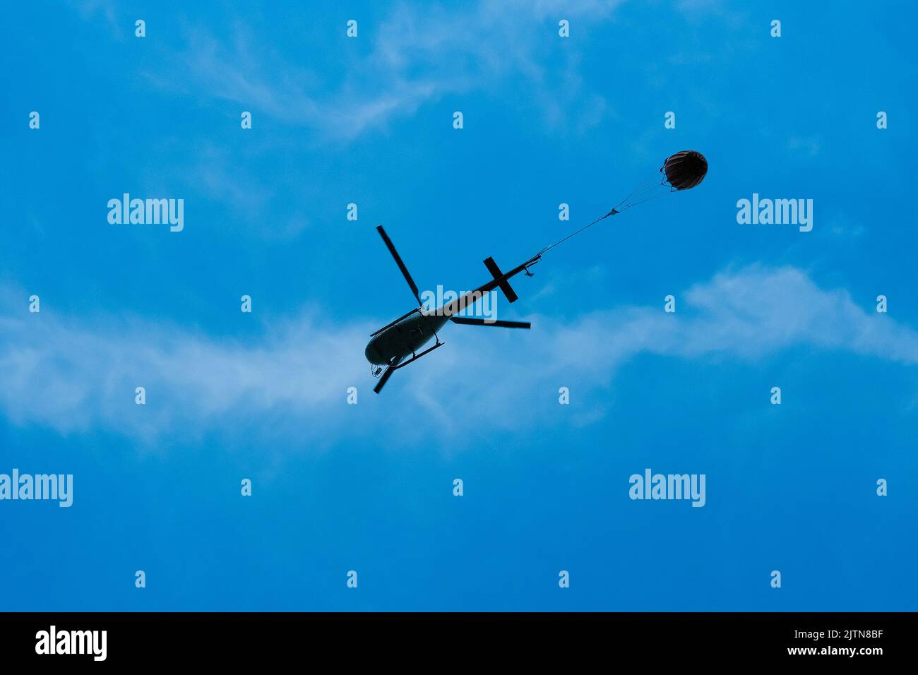 Helicopter with bag of water to put out fires flies over a forest area ...