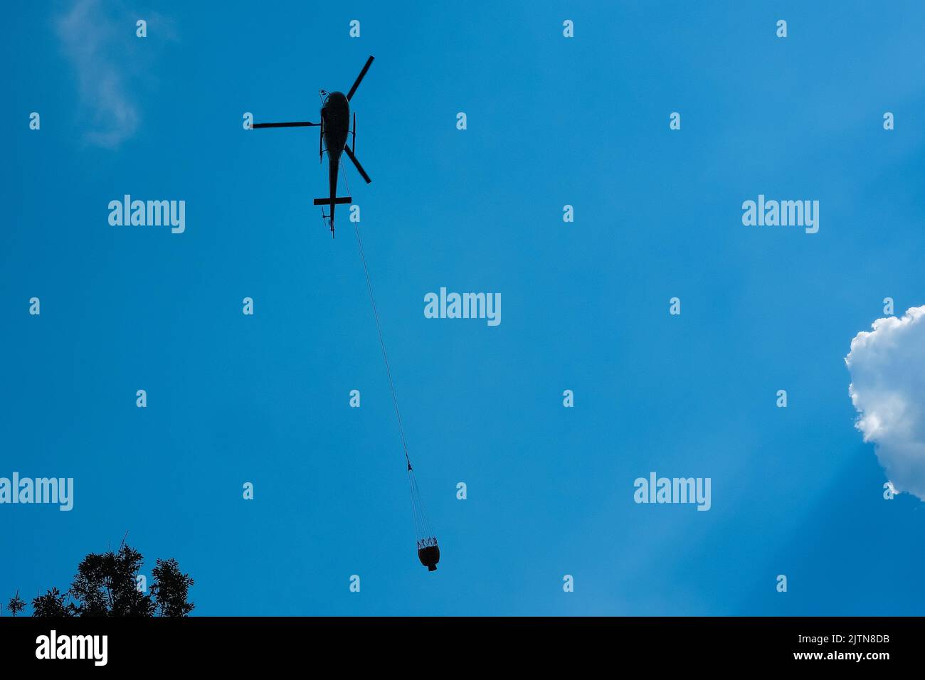 Helicopter with bag of water to put out fires flies over a forest area ...