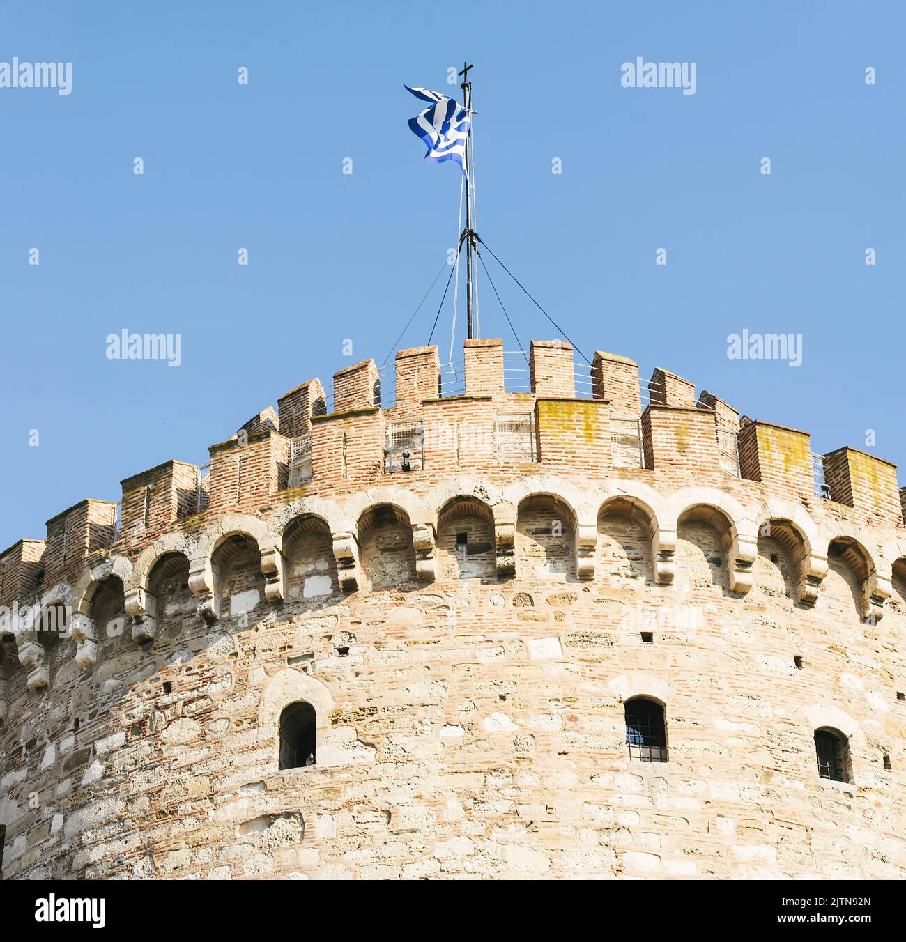 Low angle view of Iconic White Tower of Thessaloniki with waving flag ...