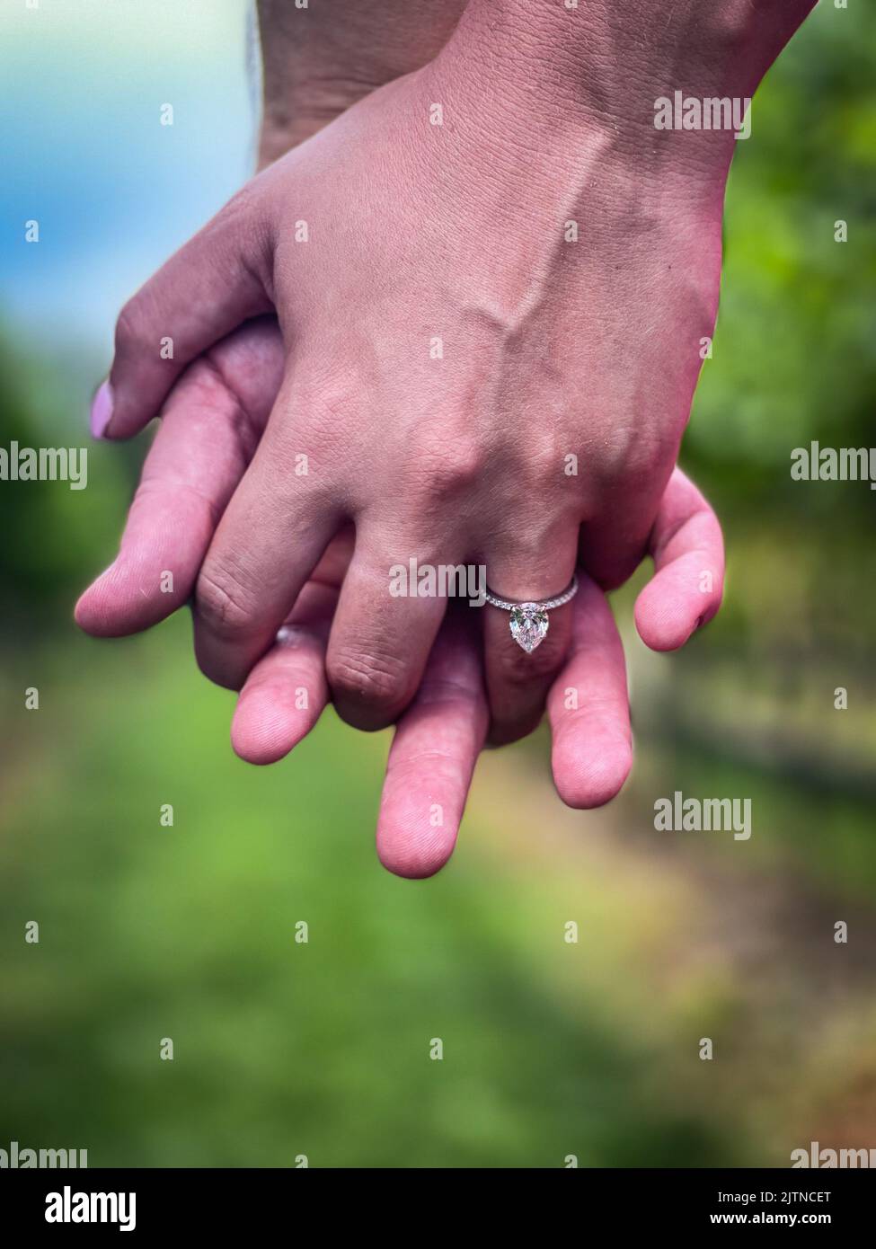 Closeup of young couple holding hands and displaying engagement ring ...