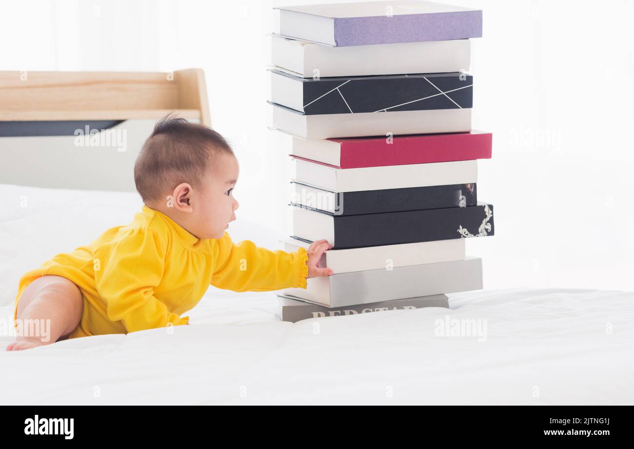Asian cute baby little girl toddler looking at a stack of books on ...