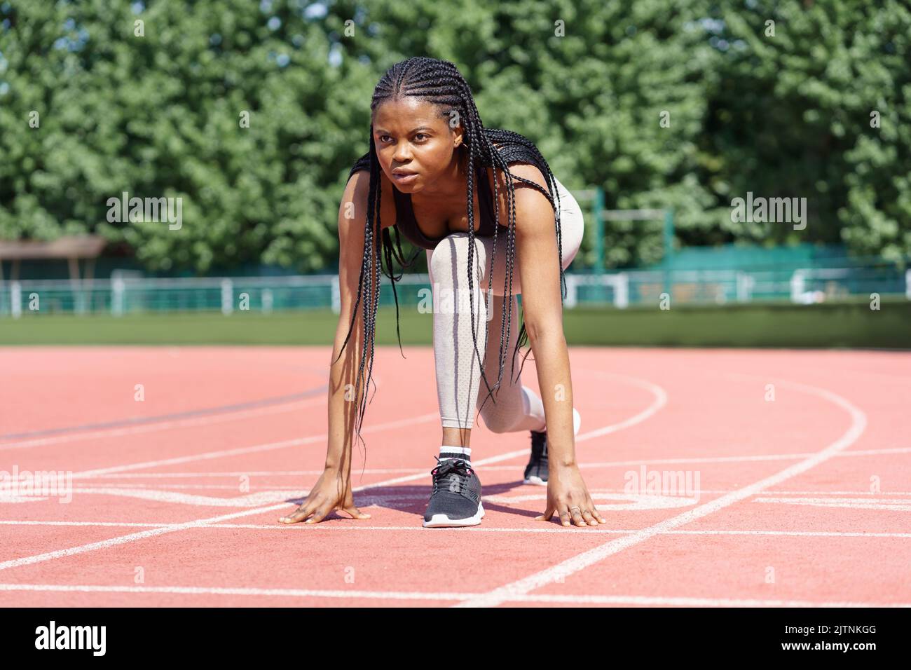 African American woman with long braids prepares low start running ...