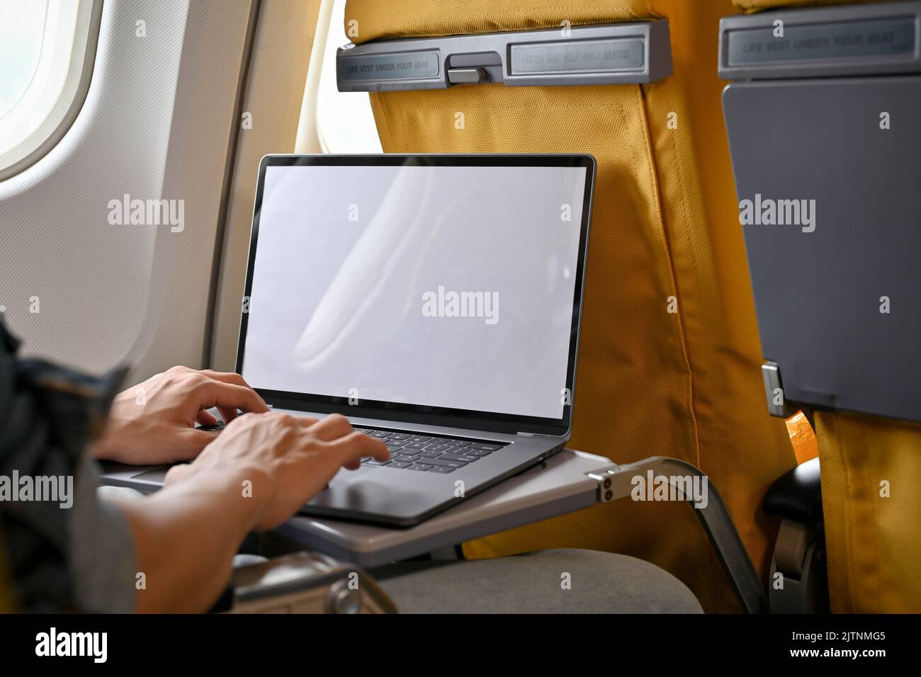 A male passenger in economy class using his portable laptop, typing on ...