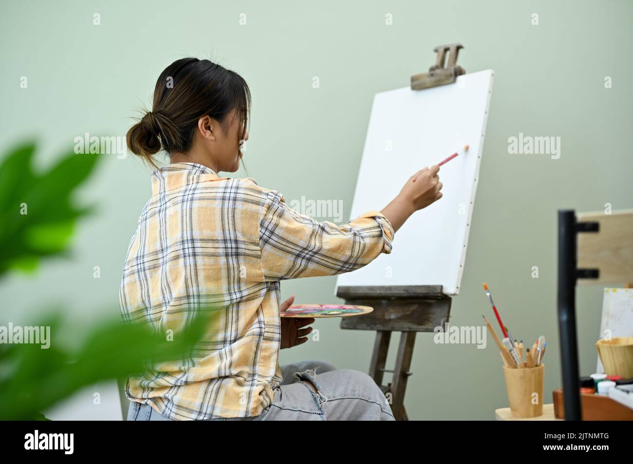 Professional young Asian female artist painting on canvas in studio ...