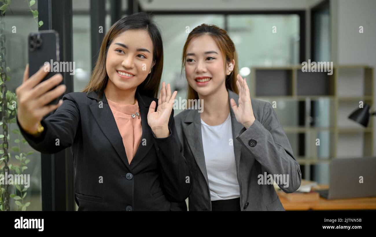 Two beautiful and pretty young asian businesswomen or office workers using a phone to take their ...