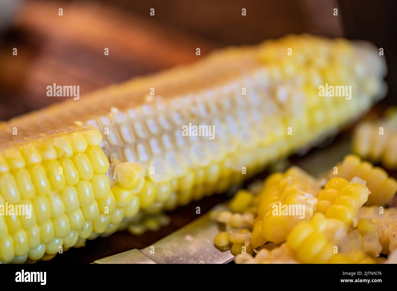 Using a knife to remove kernels from the cob of an ear of sweet corn ...