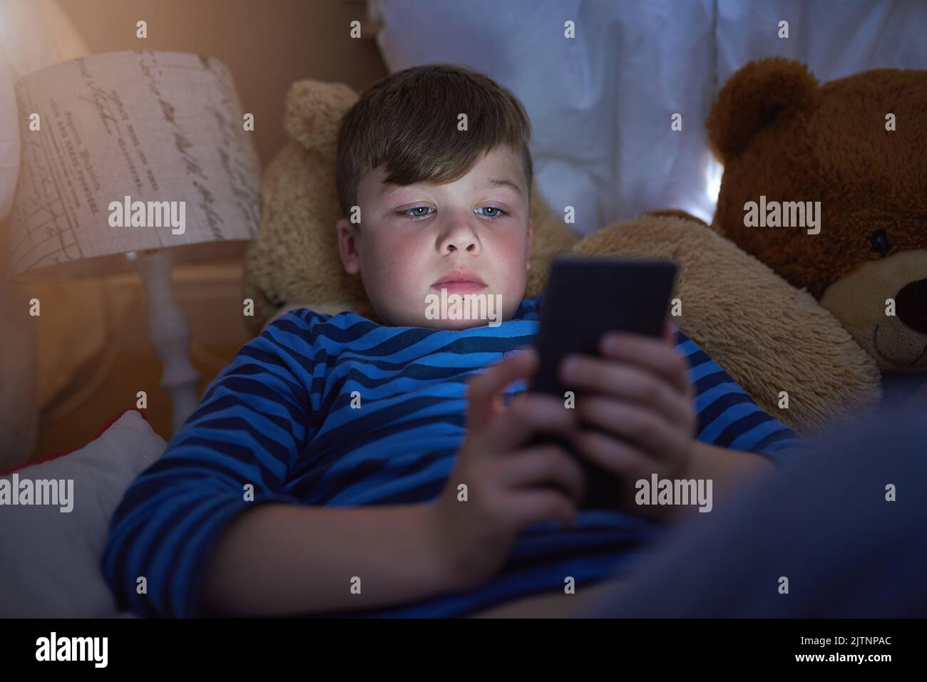 Attached to technology. a young boy using a cellphone at night in bed ...