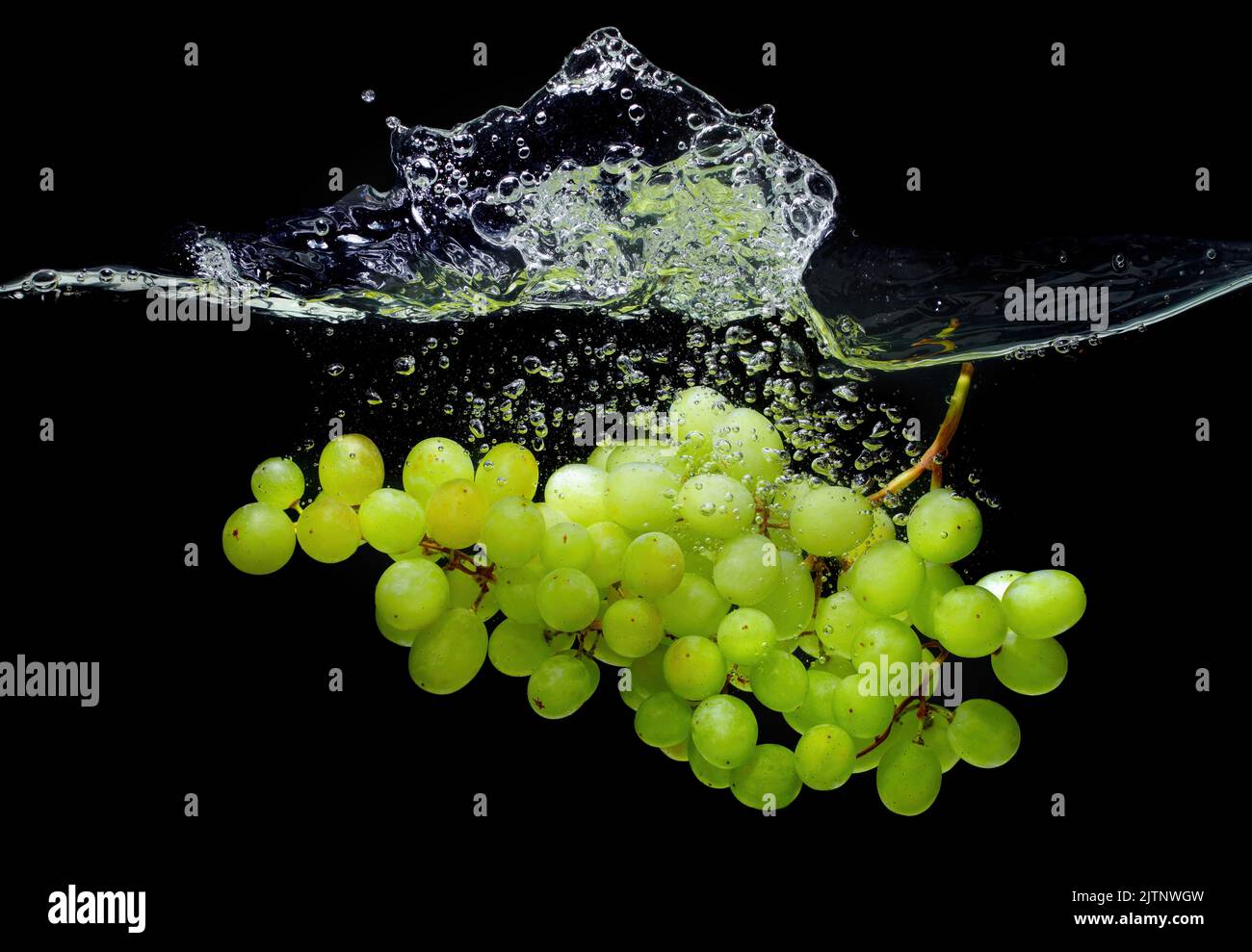 Bunch of white grapes dropped in water with splashes isolated on black ...