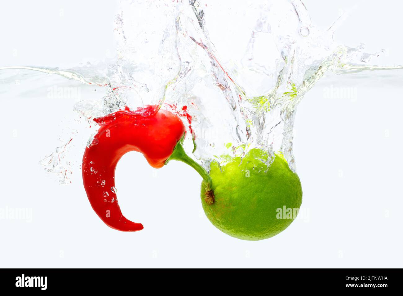 Curled red chilli and whole lime dropped in water with bubbles and ...