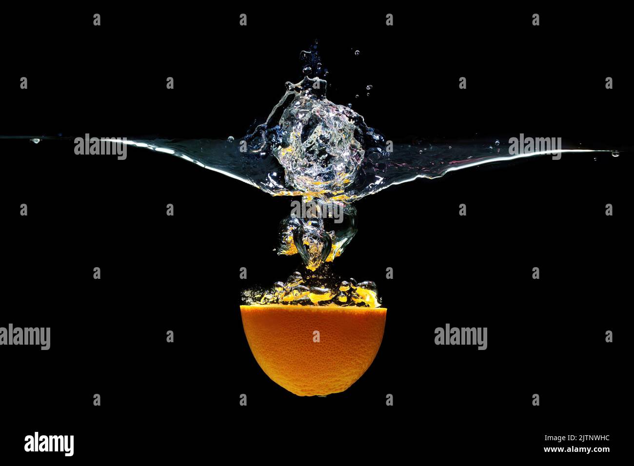 Halved orange fruit dropped in water with splashes isolated on black ...