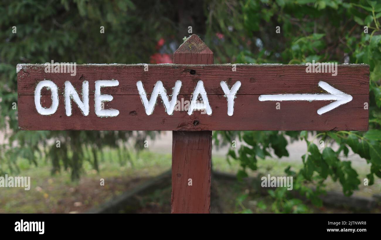 A closeup of a white font "One Way" on a brown wooden sign with an ...