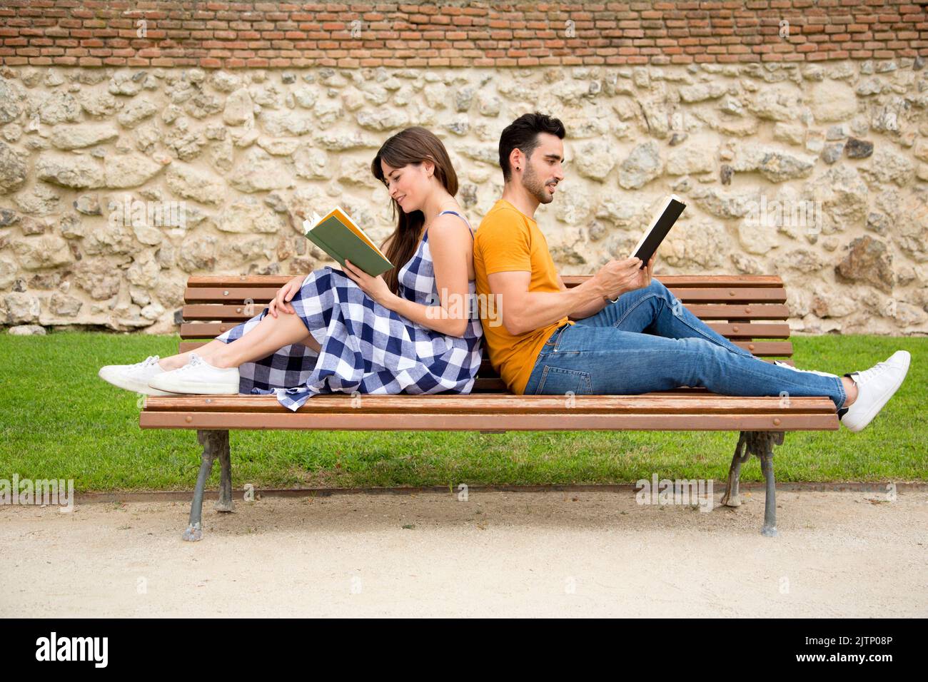 Man and woman reading books while sitting back to back in a bench of a ...
