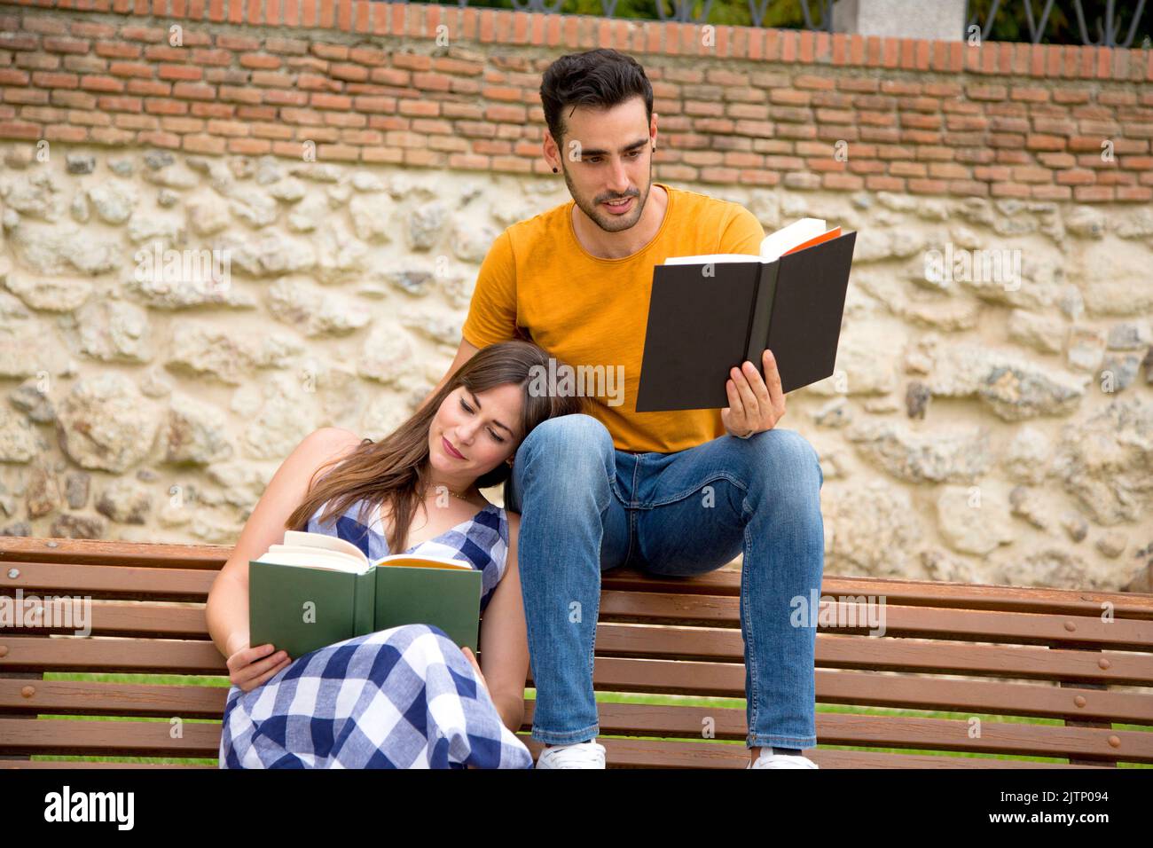 Woman leaning on her partner while reading a book sitting on a bench in ...