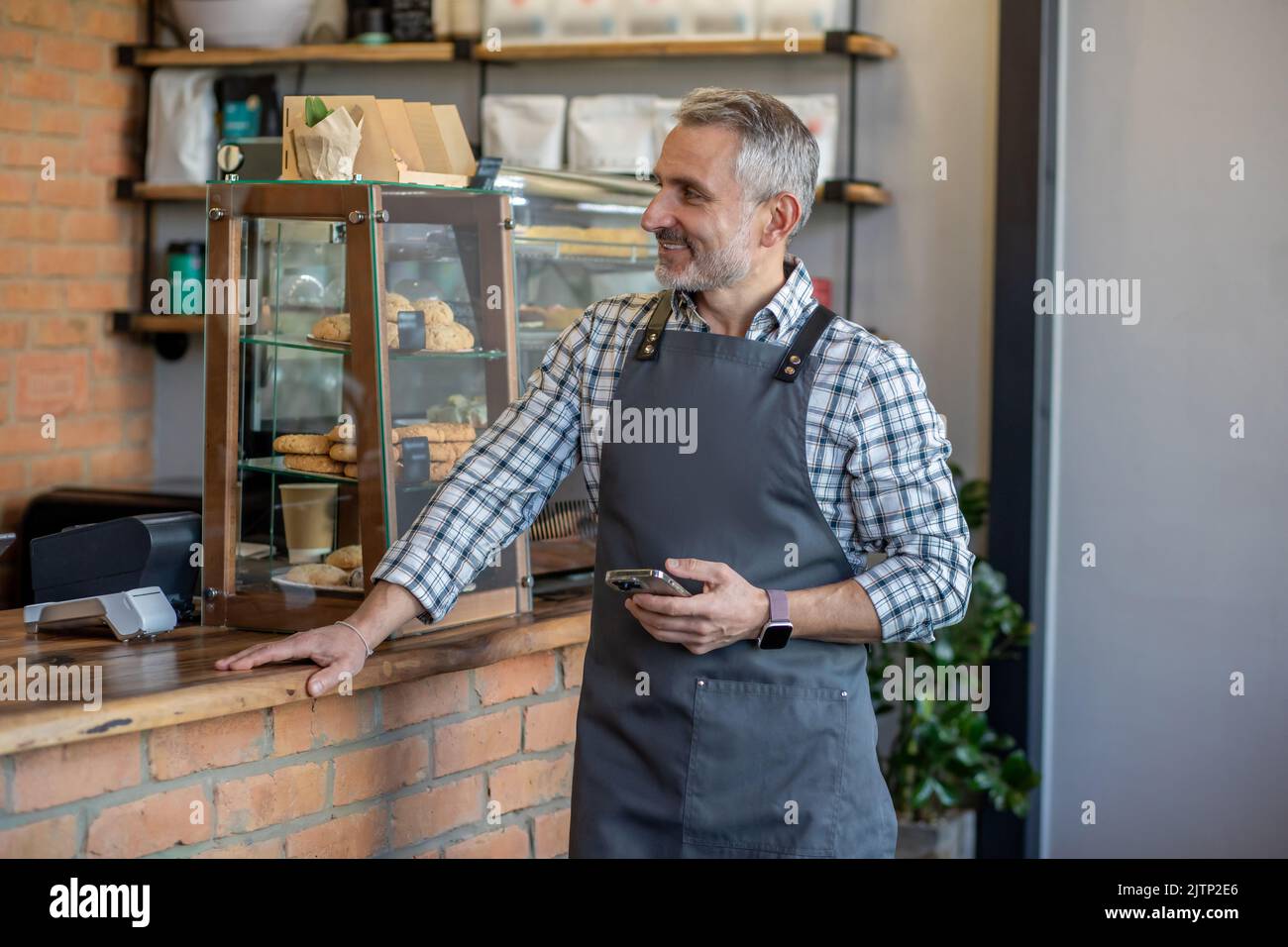 Contented pastry shop employee standing by the glass display cabinet ...