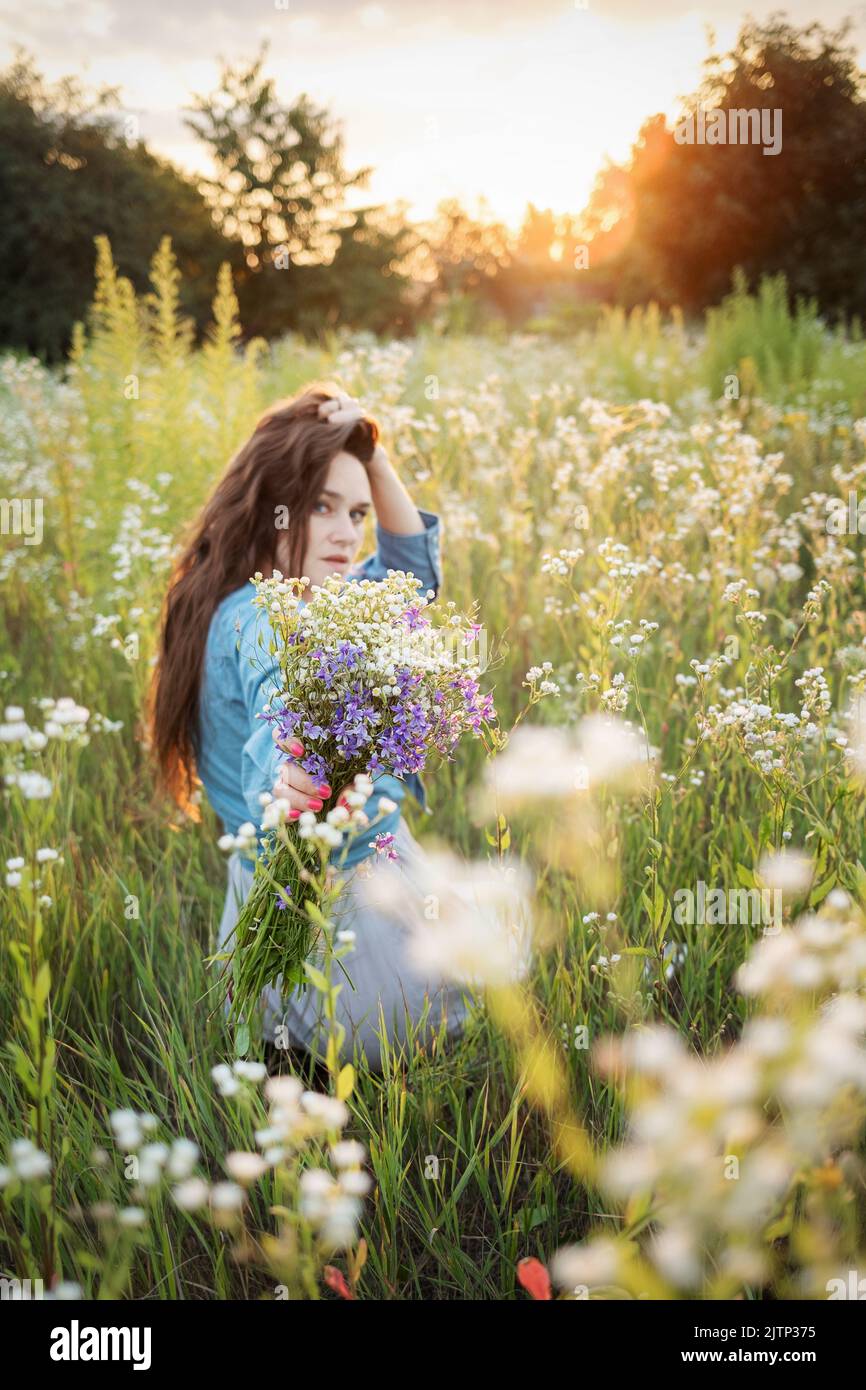 Beautiful young woman holding wildflowers bouquet and walking in flower ...