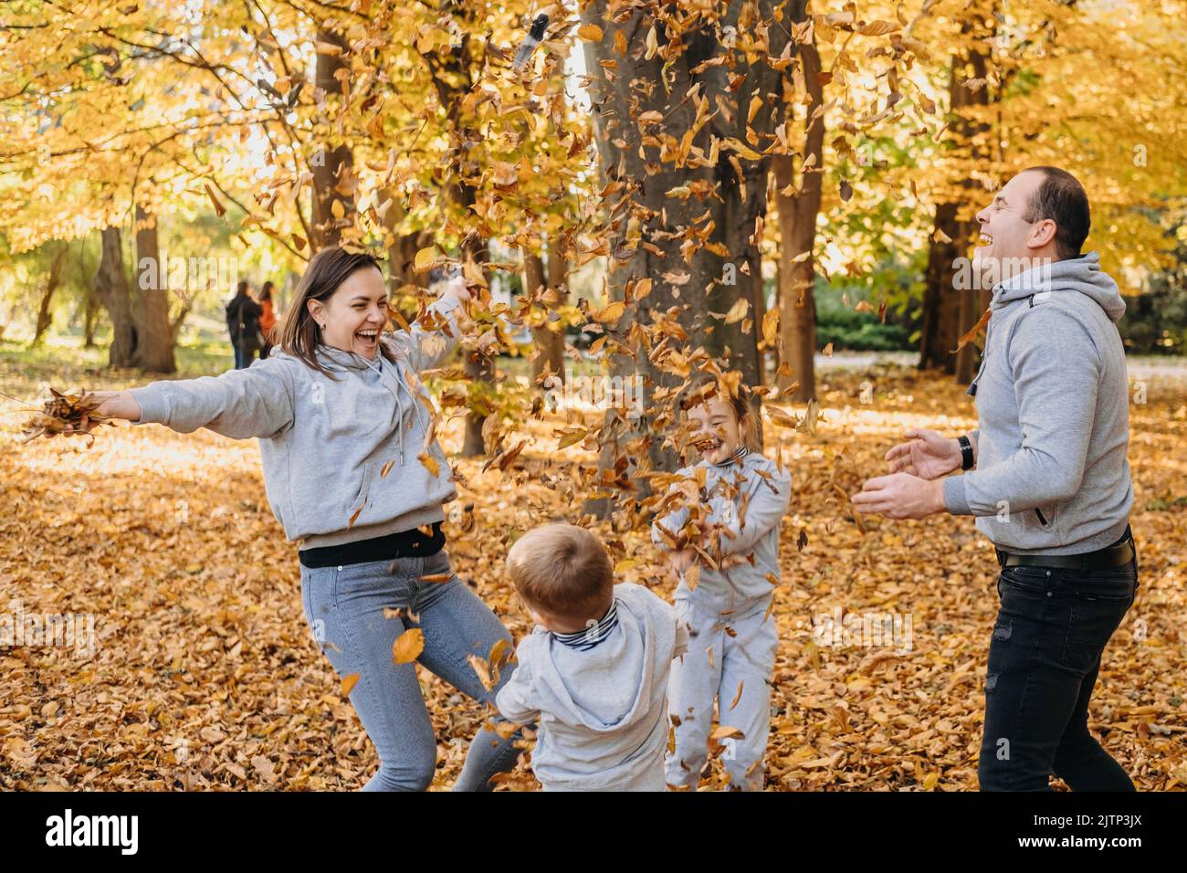 Portrait of a family with children tossing autumn leaves in park in ...