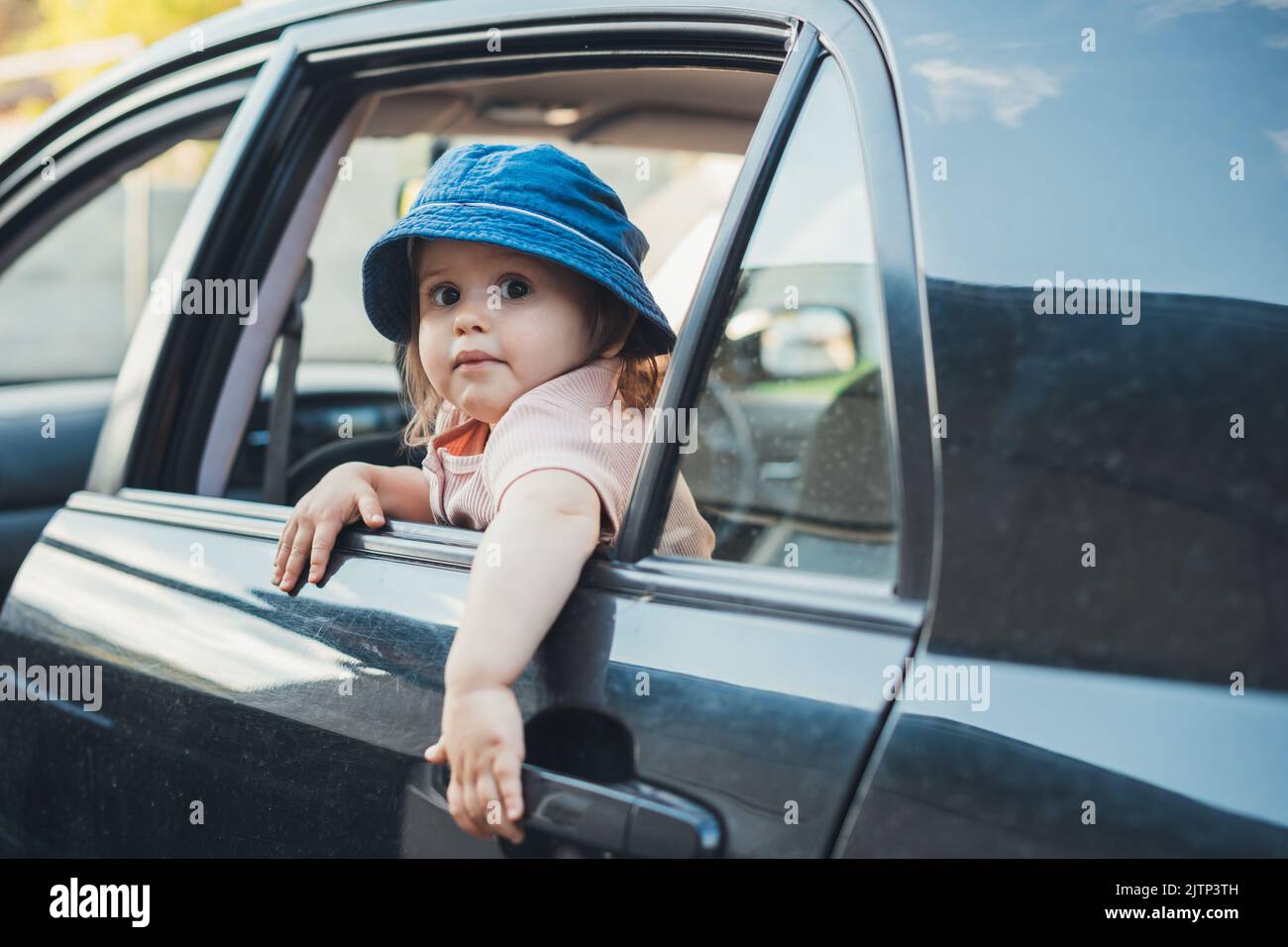 Baby girl with hat looking out the open car window seeing refreshing ...