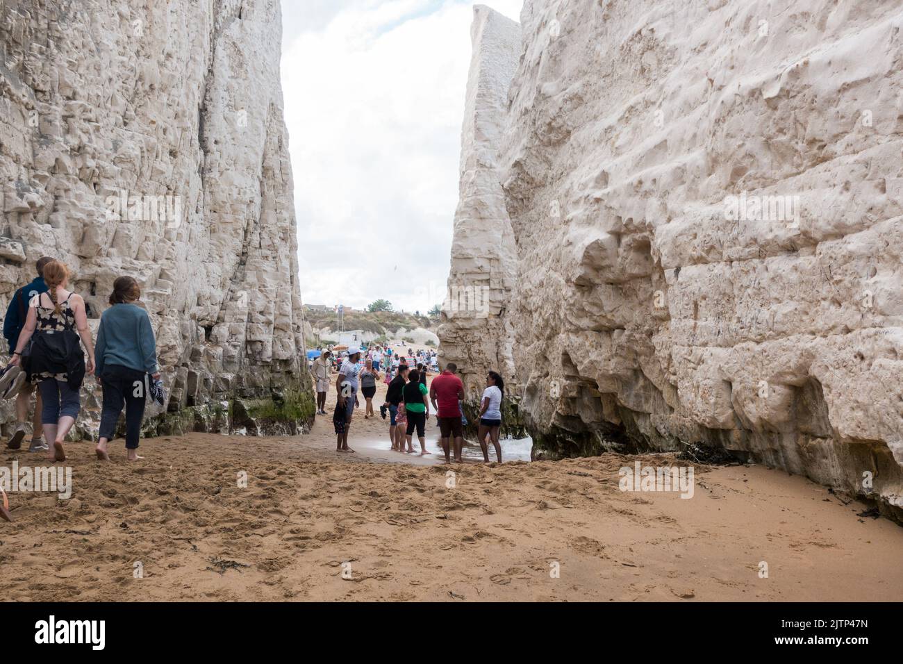 Beach goers walking in between the white chalk cliffs during low tide ...