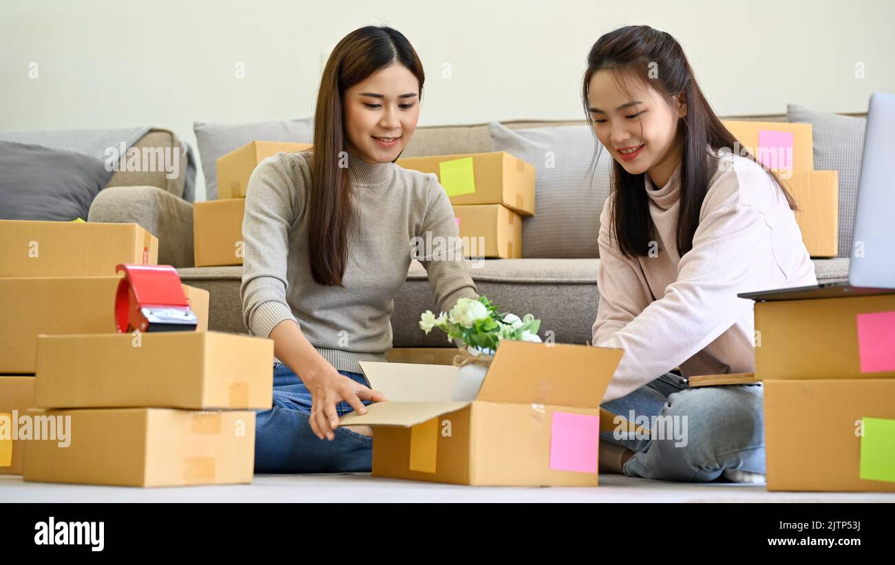 Two pretty young Asian women packing their stuff into a cardboard box ...