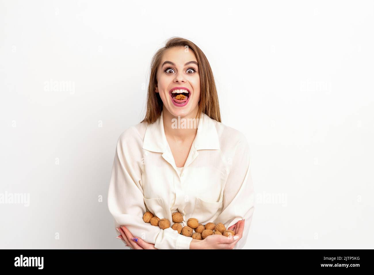 Happy young caucasian woman eating walnuts with an open mouth on white ...