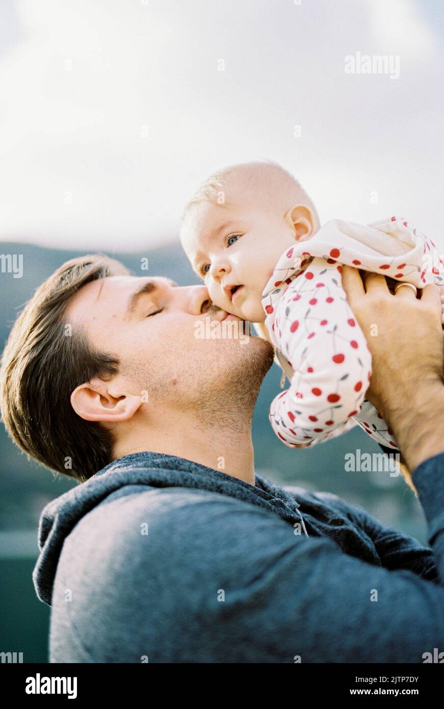 Dad lifts the baby above his head and kisses him on the cheek. Portrait ...