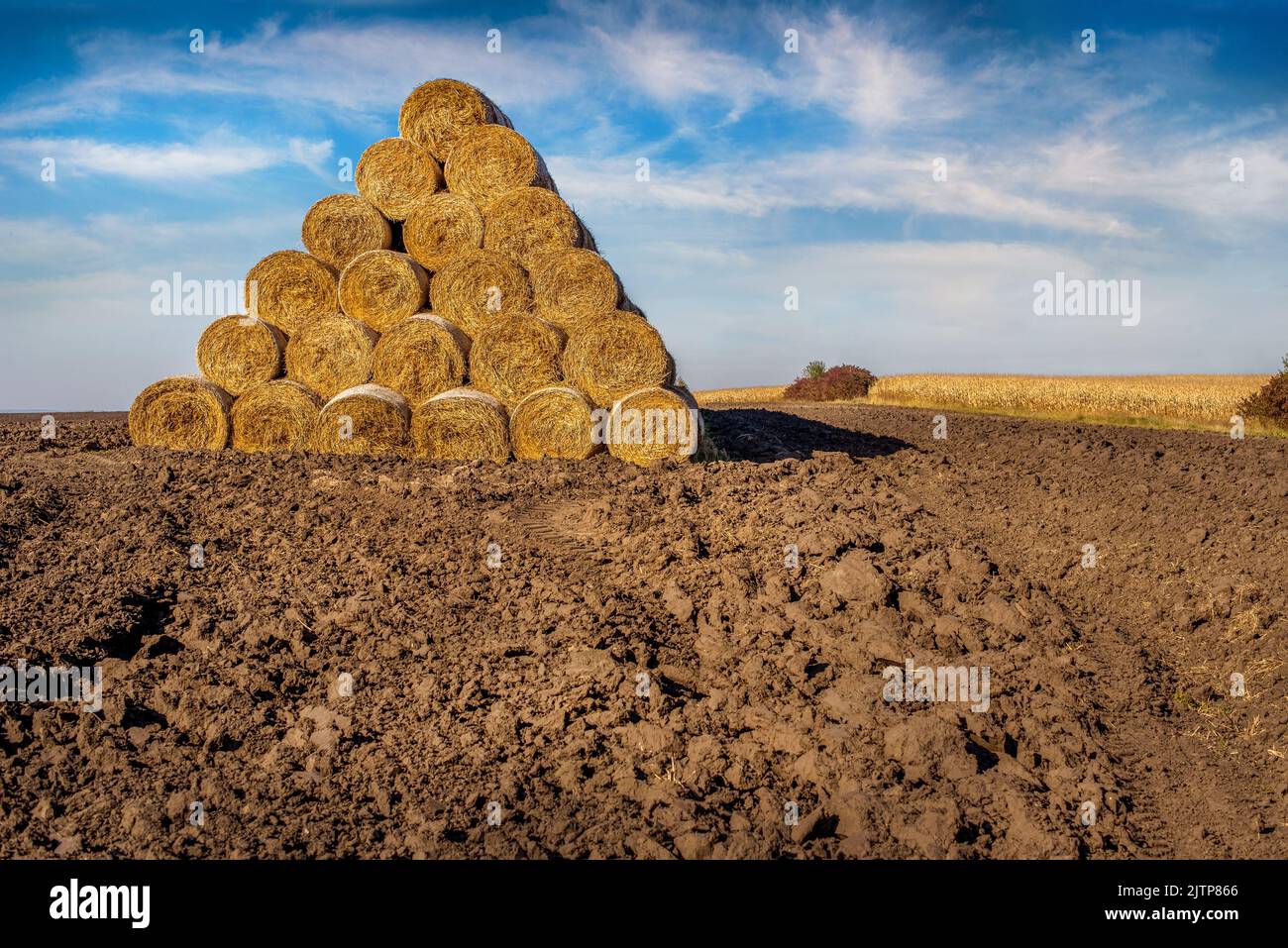 a pile of straw bales in the shape of a pyramid, stacked in a plowed ...