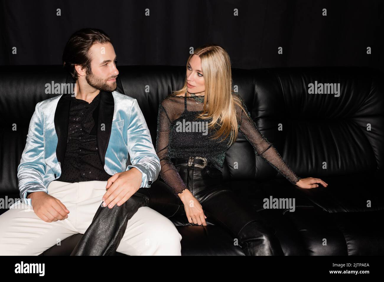 Fashionable man touching leg of blonde girlfriend on leather couch ...