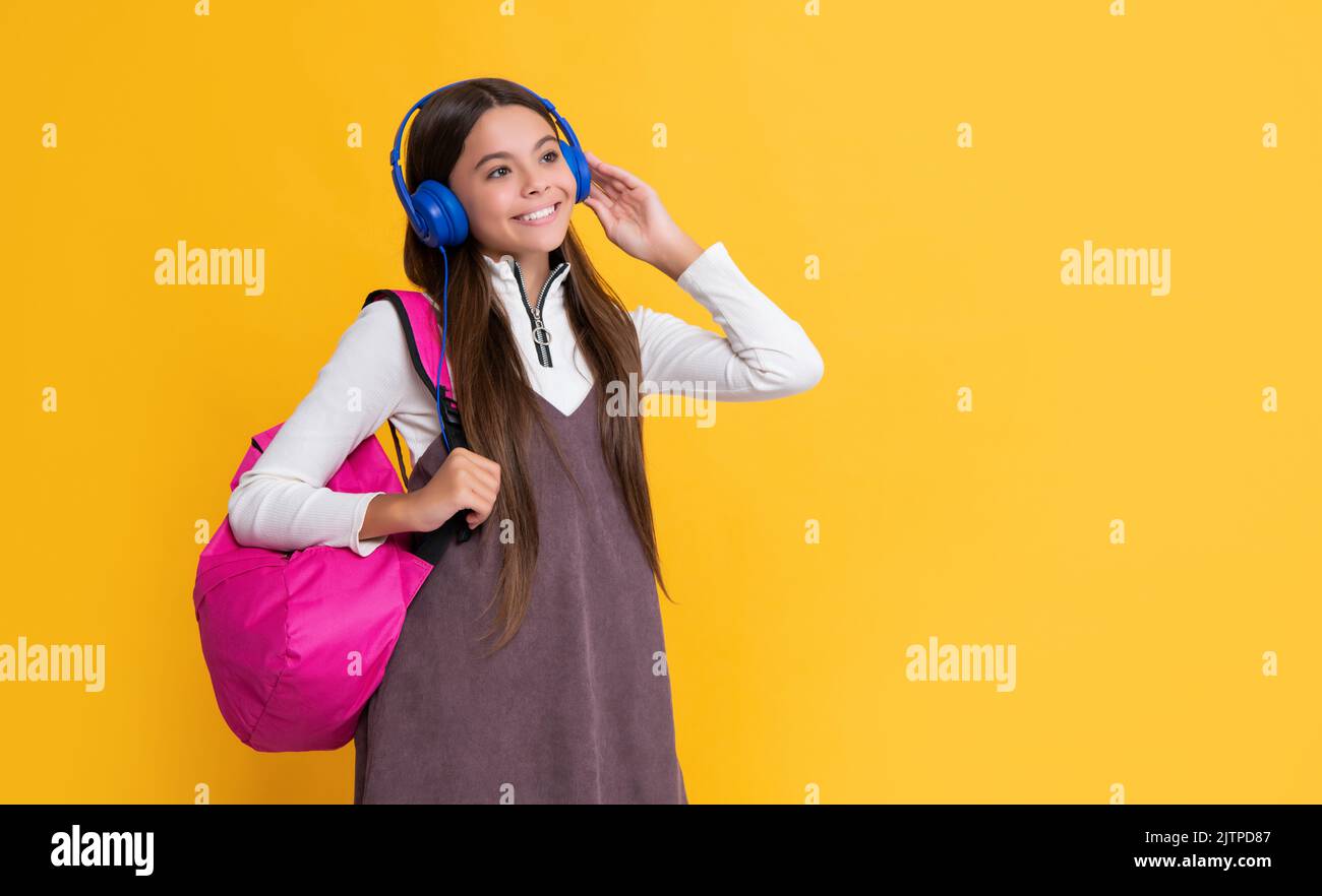 glad child in headphones with school backpack on yellow background ...