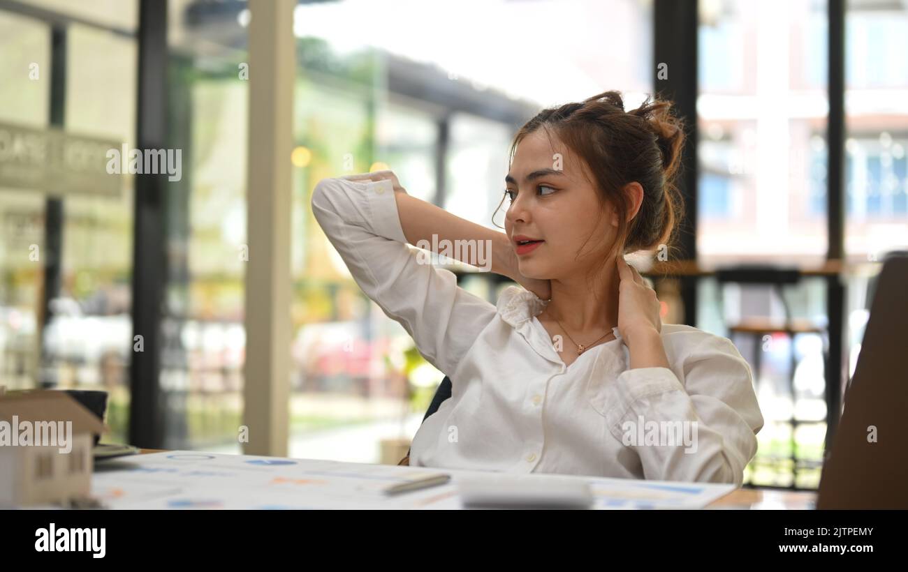 Asian female employee relaxing at work, reclining back in chair and ...