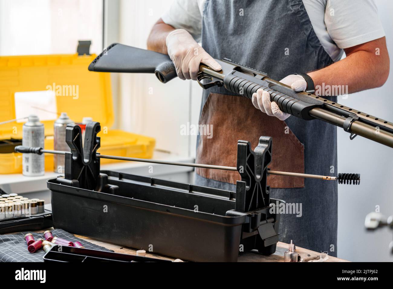 Close up of young man in apron disassembling a gun above the table ...