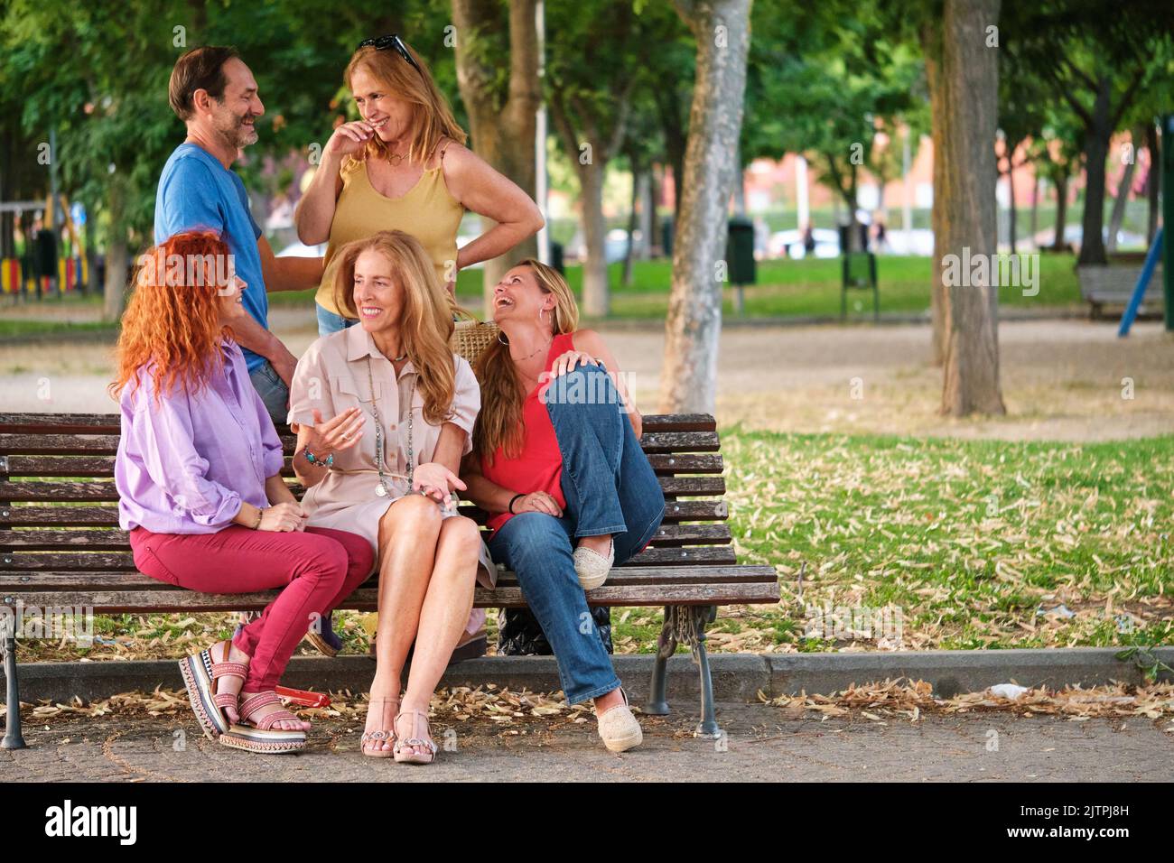 Five mature adults talking and laughing sitting on a bench in a park ...