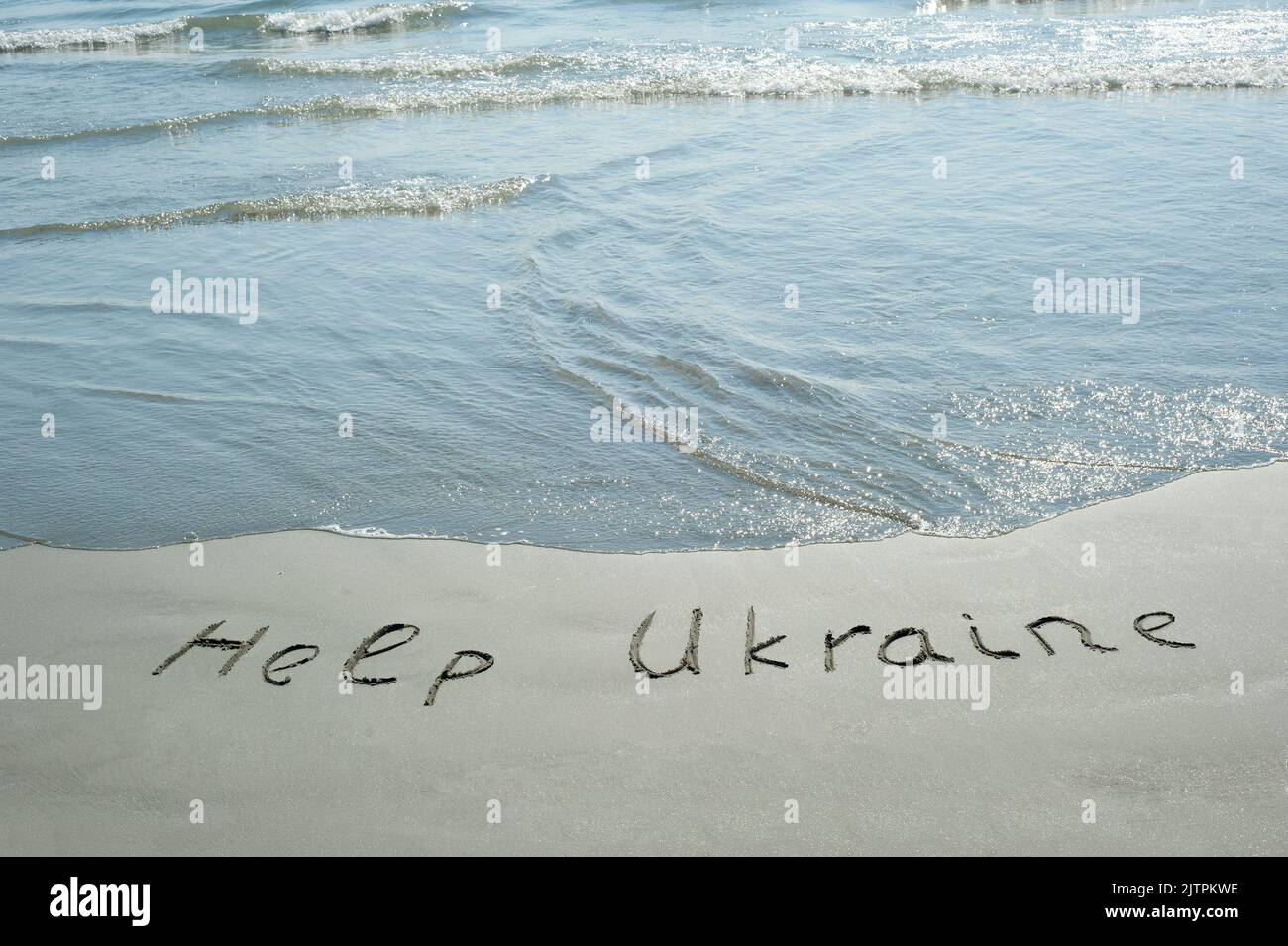 Concept or conceptual Help Ukraine handwritten text in sand on a beach ...