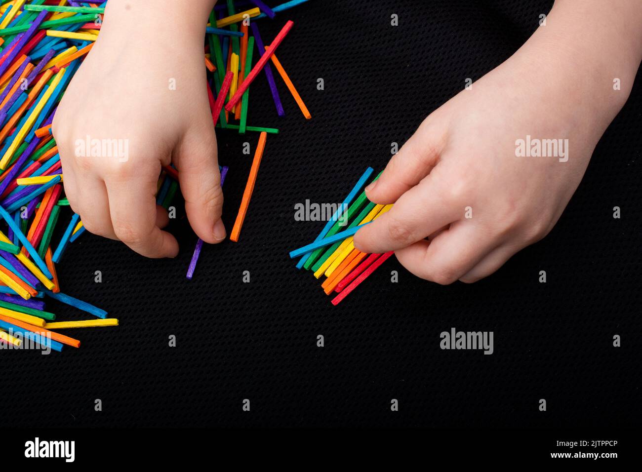 Kid playing with coloured wooden sticks for creativity on white ...
