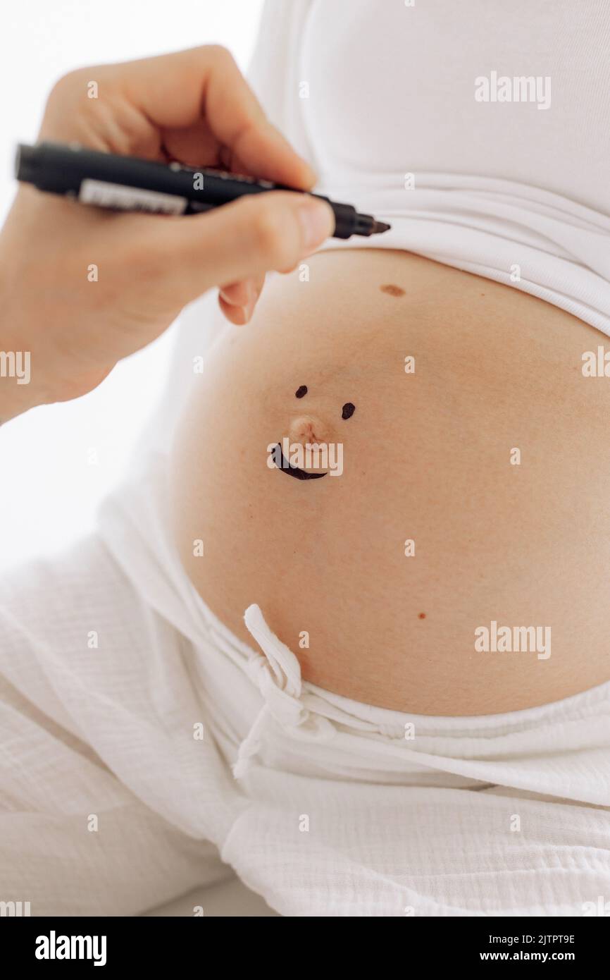 Couple parents has fun and draws smiley with felt pen on pregnant belly ...