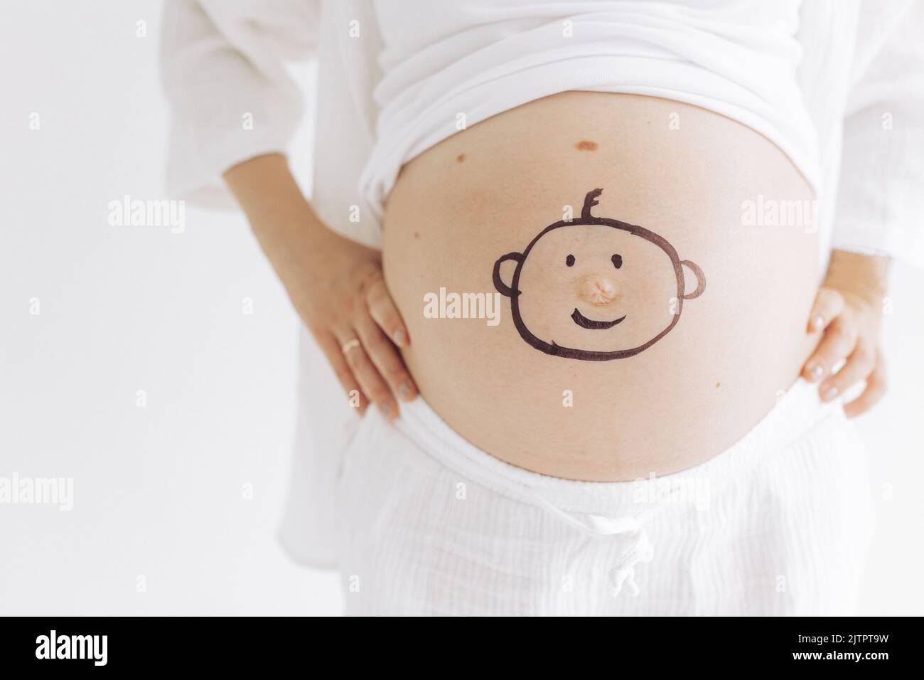Closeup view pregnant belly of woman with drawn smiling baby face on it ...