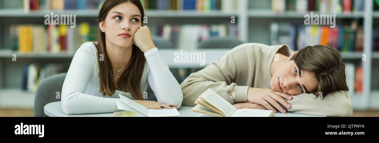 bored guy looking at camera near pensive teenage girl in reading room ...
