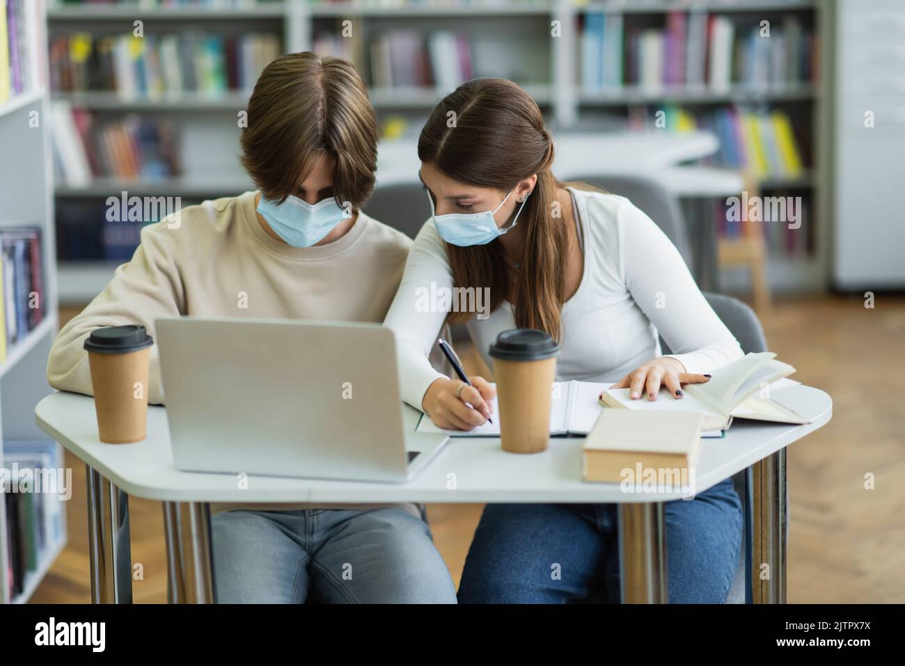 teenage students in medical masks studying near laptop in library ...