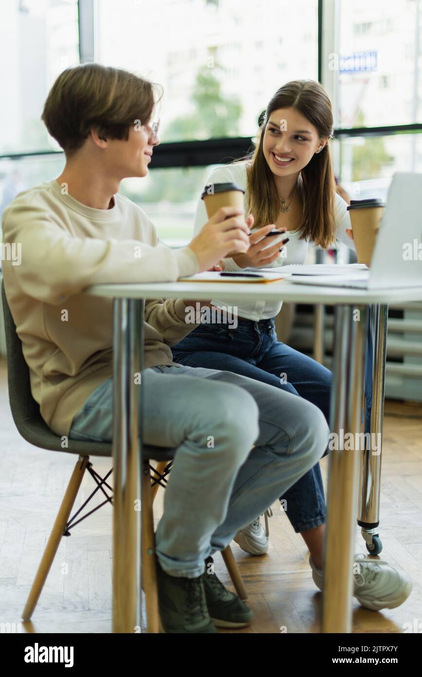 happy teenage girl talking to friend near laptop in library reading ...