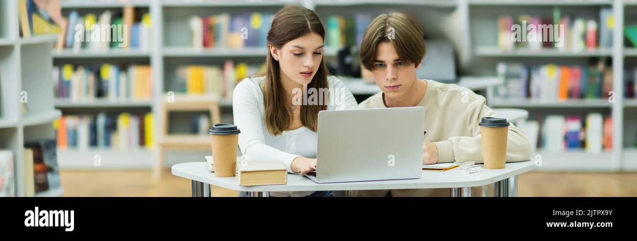 teenage friends looking at laptop while studying in library reading ...